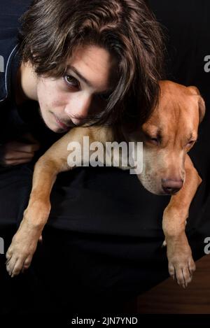 Portrait of a young man with a caramel colored pitbull dog against ...