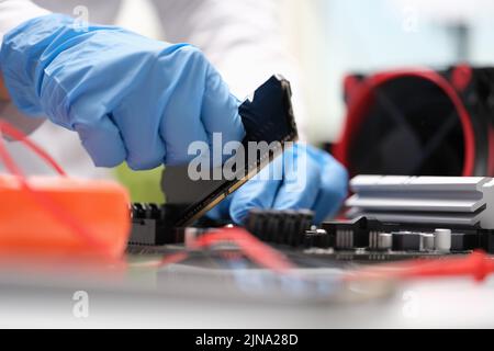 Repair engineer holds RAM chip with hands and inserts RAM of computer ...