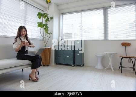 A Japanese woman checking smartphone by remote work in the small office ...