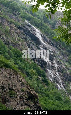 a waterfall and river pour through steep-sided rock gorge with white ...