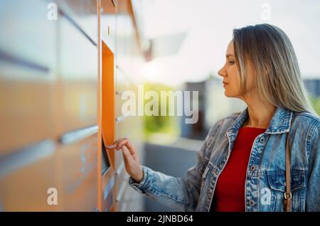 Woman picks up mail from automated self-service post terminal machine ...