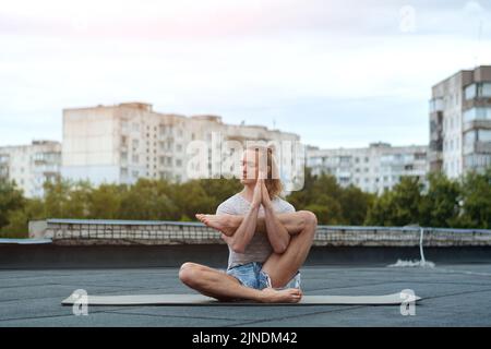 A man practices yoga on the roof of the house. Yoga at sunset. Healthy ...