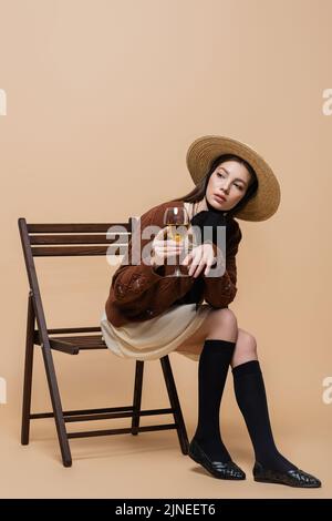Trendy woman in cardigan and straw hat holding ripe apple while sitting ...