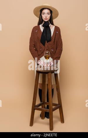 Trendy woman in cardigan and straw hat holding ripe apple while sitting ...