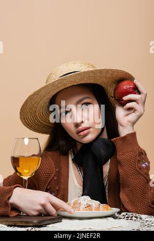 Trendy woman holding wine near apples and croissant on table isolated ...
