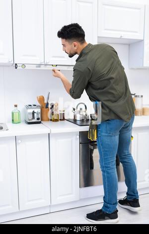 Arabian man measuring kitchen cupboard with spirit level at home ...
