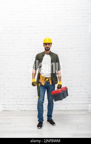 Young muslim handyman in helmet and tool belt looking at camera at home ...