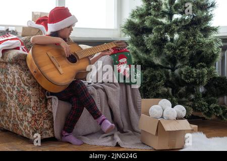 Child playing the guitar and singing near a christmas tree Stock Photo ...