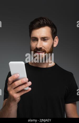 Pleased grey man using mobile phone while working with computer in ...