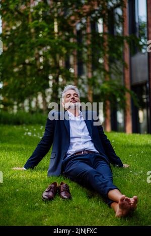 Mature businessman resting and sitting barefoot in park, feeling free ...