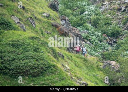 two trekkers passing in front of a massive mountain-side boulder Stock ...