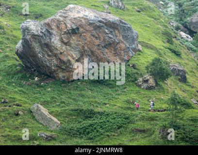 two trekkers passing in front of a massive mountain-side boulder Stock ...