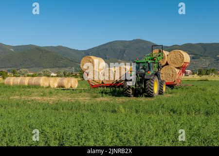 A tractor lifts hay bales to align them on a trailer in the countryside ...