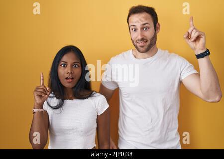 Interracial couple standing over yellow background smiling cheerful ...