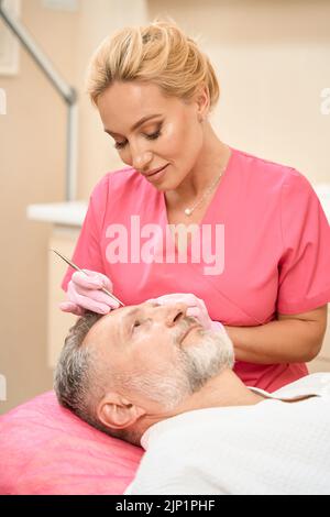 Beautician cleans face with spoon uno skin under lamp magnifying Stock ...
