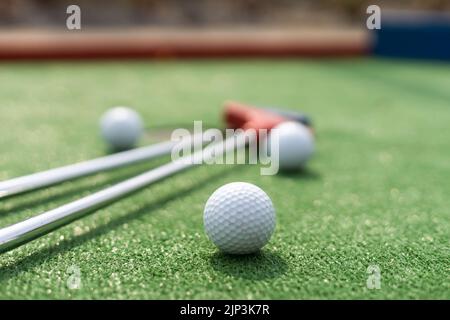 Mini-golf clubs and balls of different colors laid on artificial grass ...