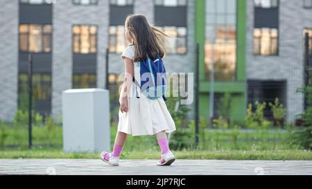 Preschooler girl with schoolbag walks past school building Stock Photo ...