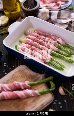 ceramic baking dish for cooking aspargus covered with bacon on wooden ...