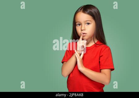 beautiful little girl asking to be quiet with finger on lips on beige ...