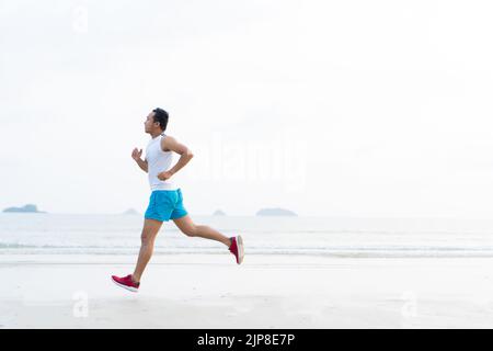 asian sport man running along seaside. running on beach with healthy ...