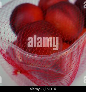 Nectarines in a plastic box with a net. Supermarket packaging. Too much ...
