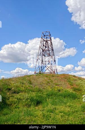 Silhouette of metal geodetic tower is on hillock on cloudy sky ...