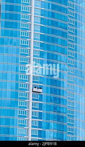 A glass building wall with window washers descending the facade on a ...