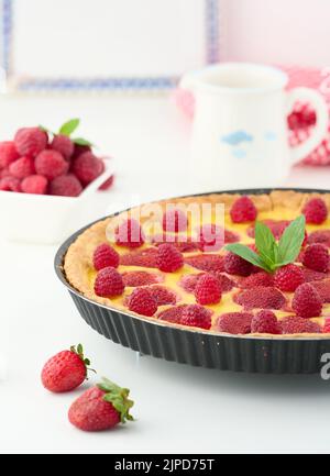 Round quiche with red strawberries and raspberries on a white table ...