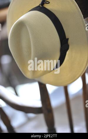 Mans hat with black band hanging on the back of a ladder back wooden ...