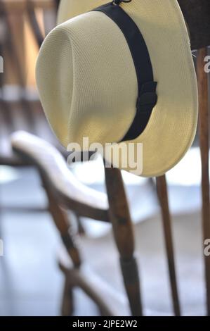 Mans hat with black band hanging on the back of a ladder back wooden ...