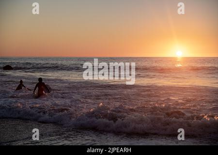 Two surfer going into the Pacific Ocean at sunset in Sayulita, Mexico ...