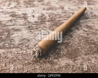 Detail of a lit marijuana or weed joint pictured on a brown wooden ...