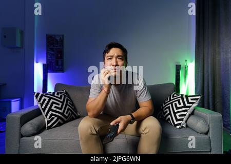 A young Southeast Asian male chilling and watching TV in the living ...
