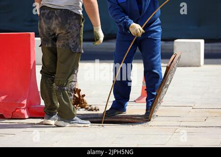 Workers over the open sewer hatch on a street Stock Photo - Alamy