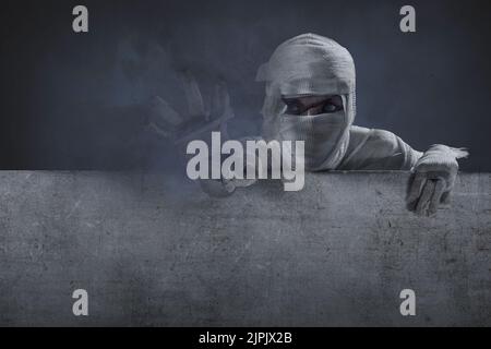 Mummy comes from behind the wall with a cemetery background. Halloween ...