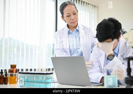 Male professor examining chemical in beaker while explaining to student ...