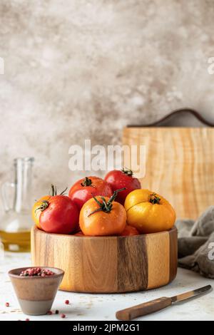 Wooden bowl of colorful tomatoes with knife, board, oil bottle and ...