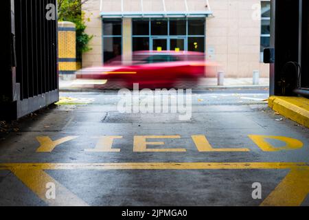 Worn yellow yield sign at the exit of a car park near Tallaght Square ...