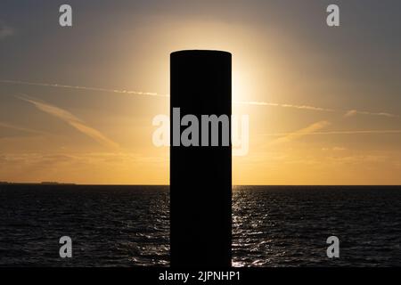 Sun setting behind a pole reflecting in the water Stock Photo - Alamy