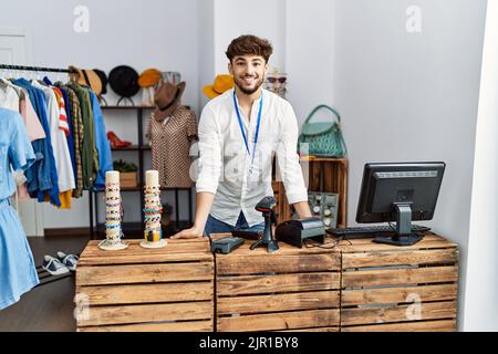 Young arab man shopkeeper smiling confident working at clothing store ...
