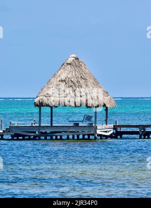 A pier and lounge chairs under a palapa facing the turquoise-blue ...
