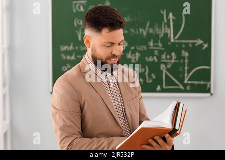Handsome Math teacher reading book in classroom Stock Photo - Alamy