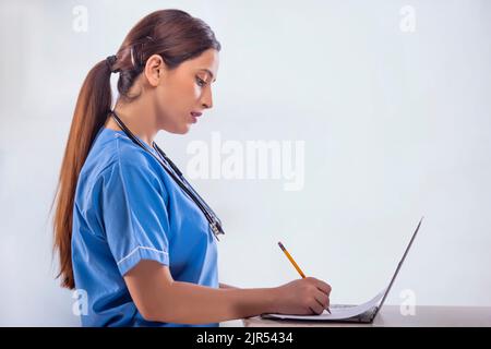 Asian healthcare worker taking notes while working on laptop computer ...