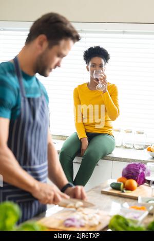 Vertical of happy diverse couple cooking together and using tablet in ...