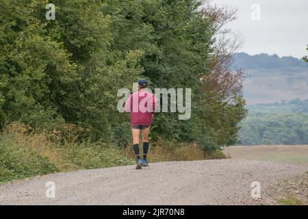 a lone man in a purple top, jogging along an unmade track road, hiking ...