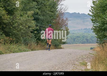 a lone man in a purple top, jogging along an unmade track road, hiking ...