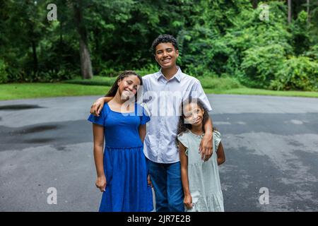 Three siblings standing outside their home hugging and embracing for a ...