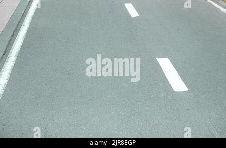 Close-up of an asphalt road with an intermittent marking line and grass ...