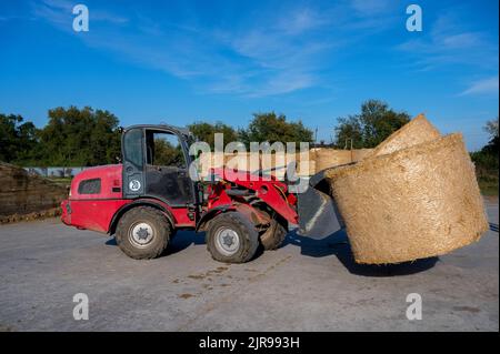 Farmer unloading round bales of straw with a front end loader Storing ...