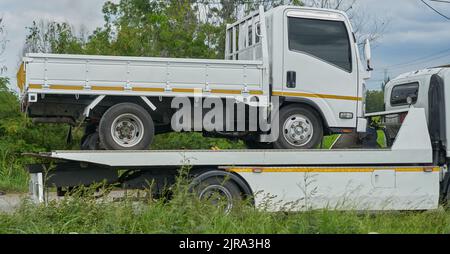 A small white truck being transported on a larger but similar looking ...